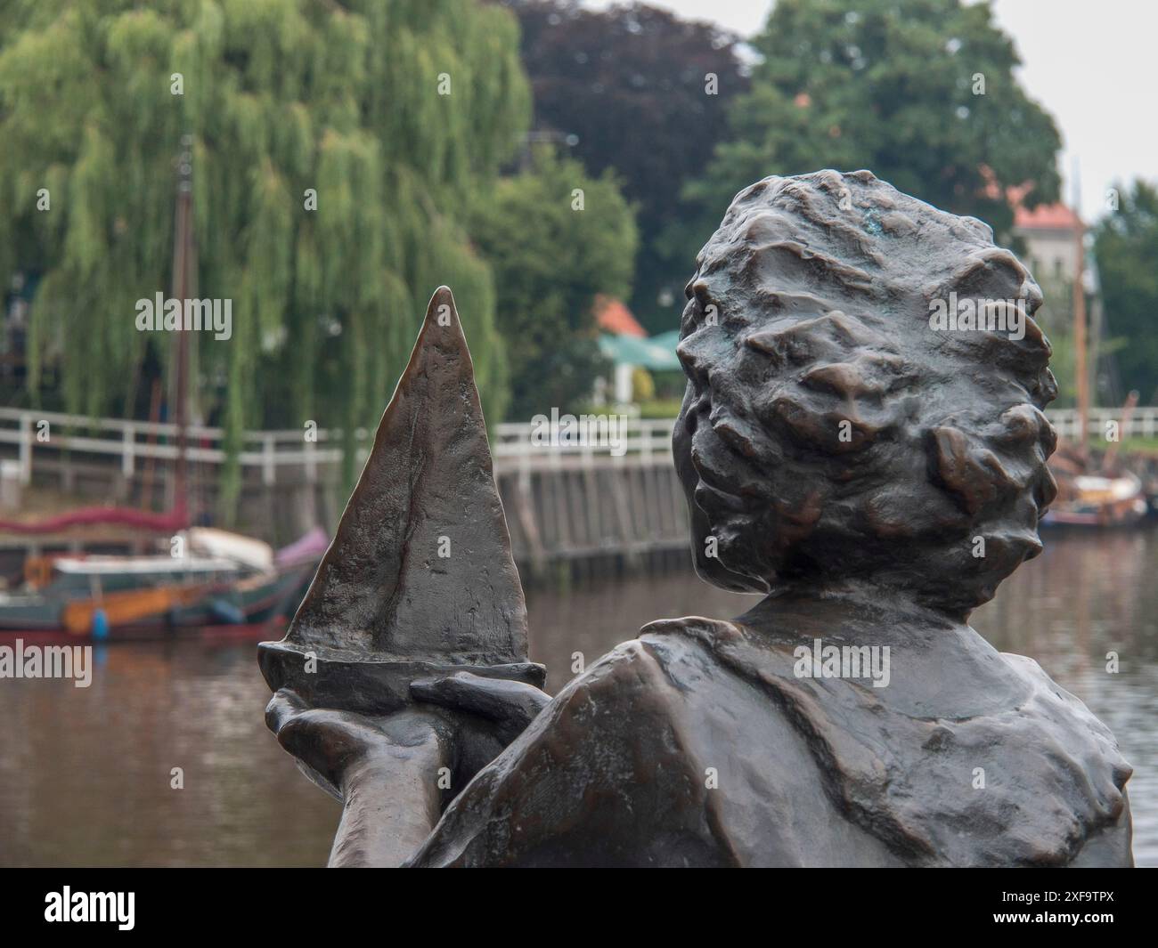Bronze statue holding a small boat with a quiet canal and nature in the ...