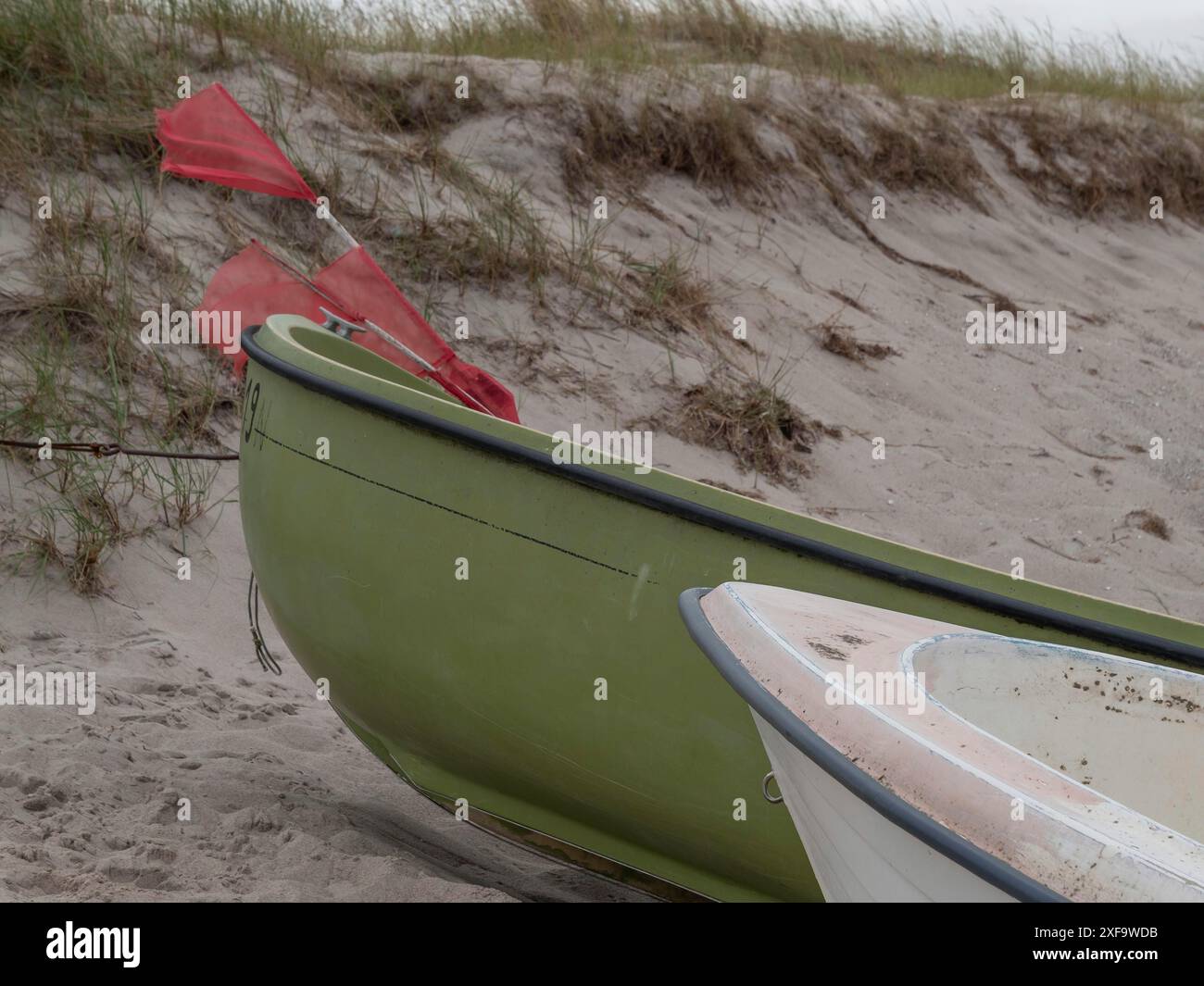 A green and white boat lying on the dune beach with red flags ...