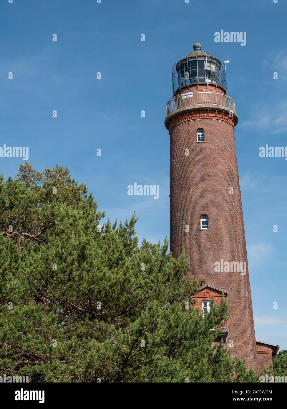 A red brick lighthouse rises next to green trees under a clear sky ...