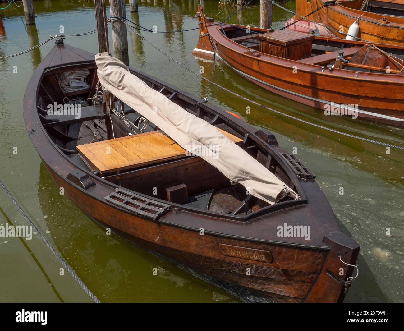 A dark wooden boat in the calm waters of the harbour with a canvas ...