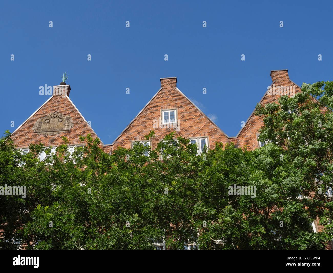 Three buildings with red bricks and a tree under a blue sky, Bremen ...