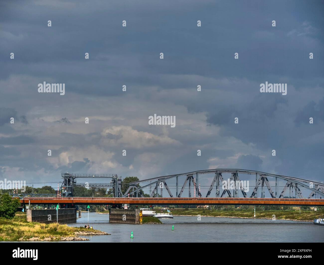 Metal bridge over a river under a cloudy sky in a quiet landscape ...