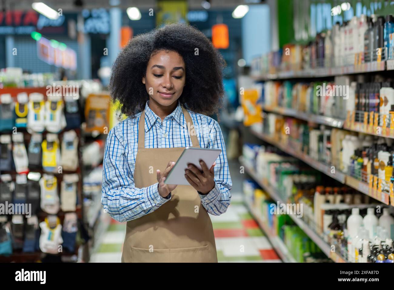 Female employee in a retail store aisle, using a tablet for inventory ...