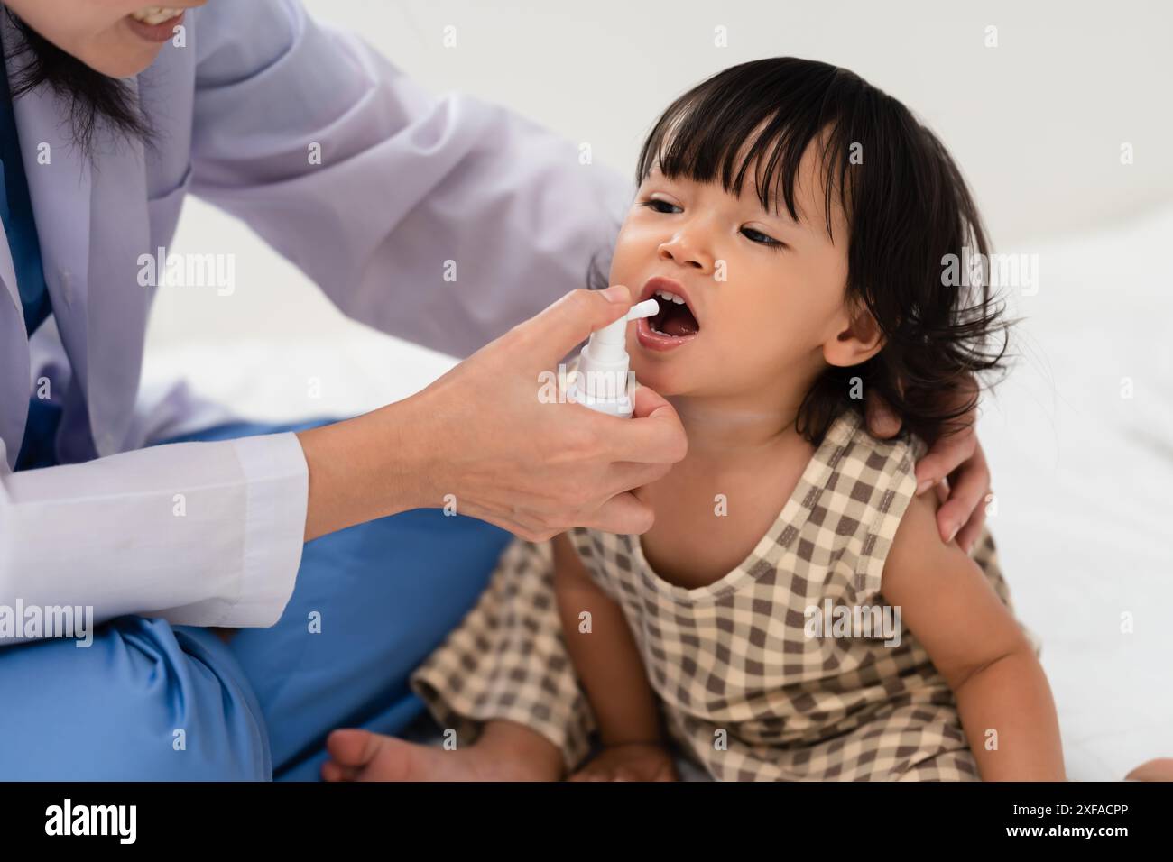 Doctor Spraying Medicine In Mouth Of Toddler Girl Baby Sore Throat doctor-spraying-medicine-in-mouth-of-toddler-girl-baby-sore-throat