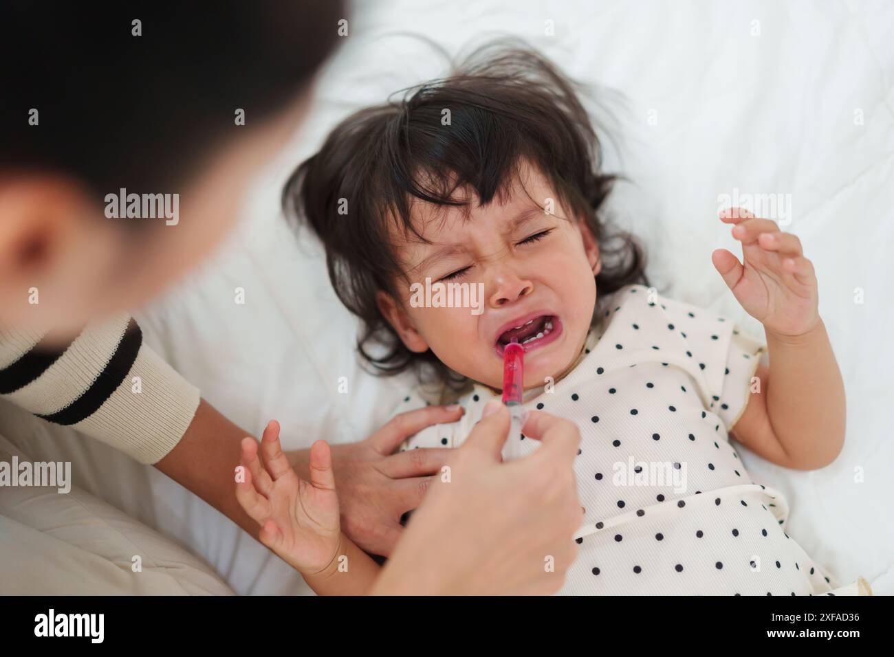 mother feeding a liquid medicine to baby girl by syringe. sick crying ...