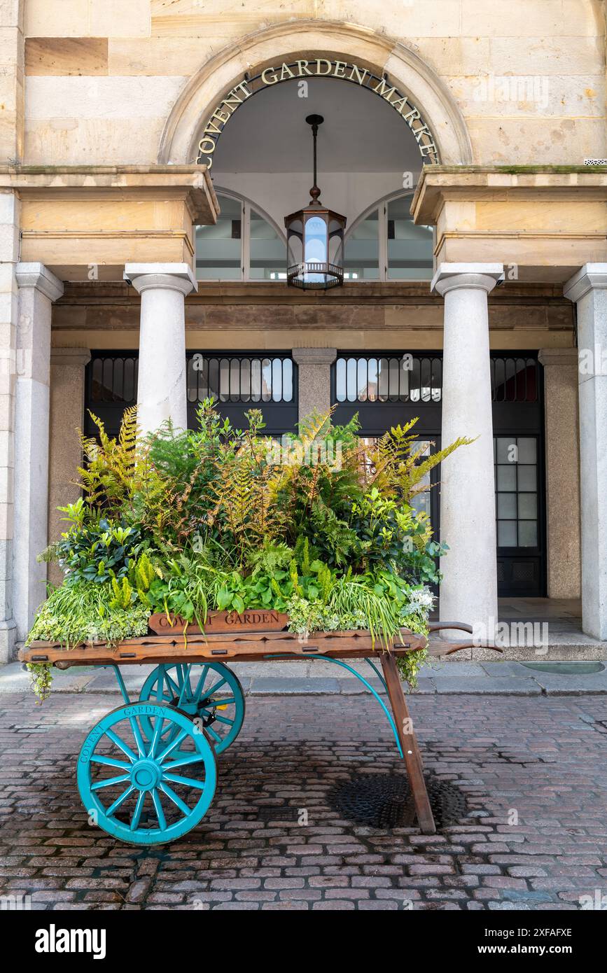 Old fashioned wooden barrow with boxes of flowers, outside the stores ...