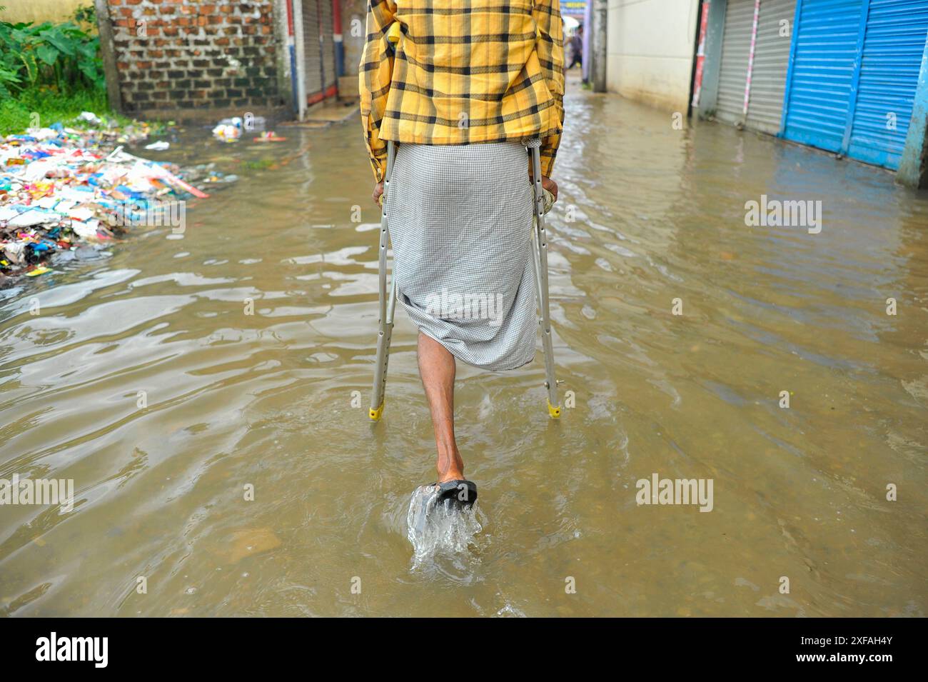 A disabled man with his stretcher wades through flooded water in the ...