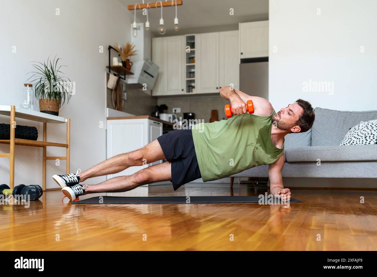 Male person doing anaerobic workout at home, lifting dumbbell in side ...