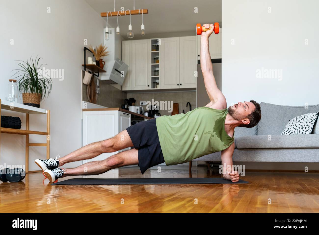 Man does anaerobic workout at home, lifting dumbbell in side plank ...