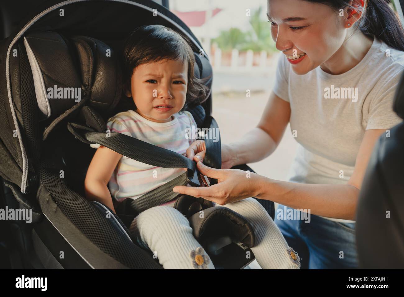 mother is fastening safety belt to crying toddler girl in a car seat ...