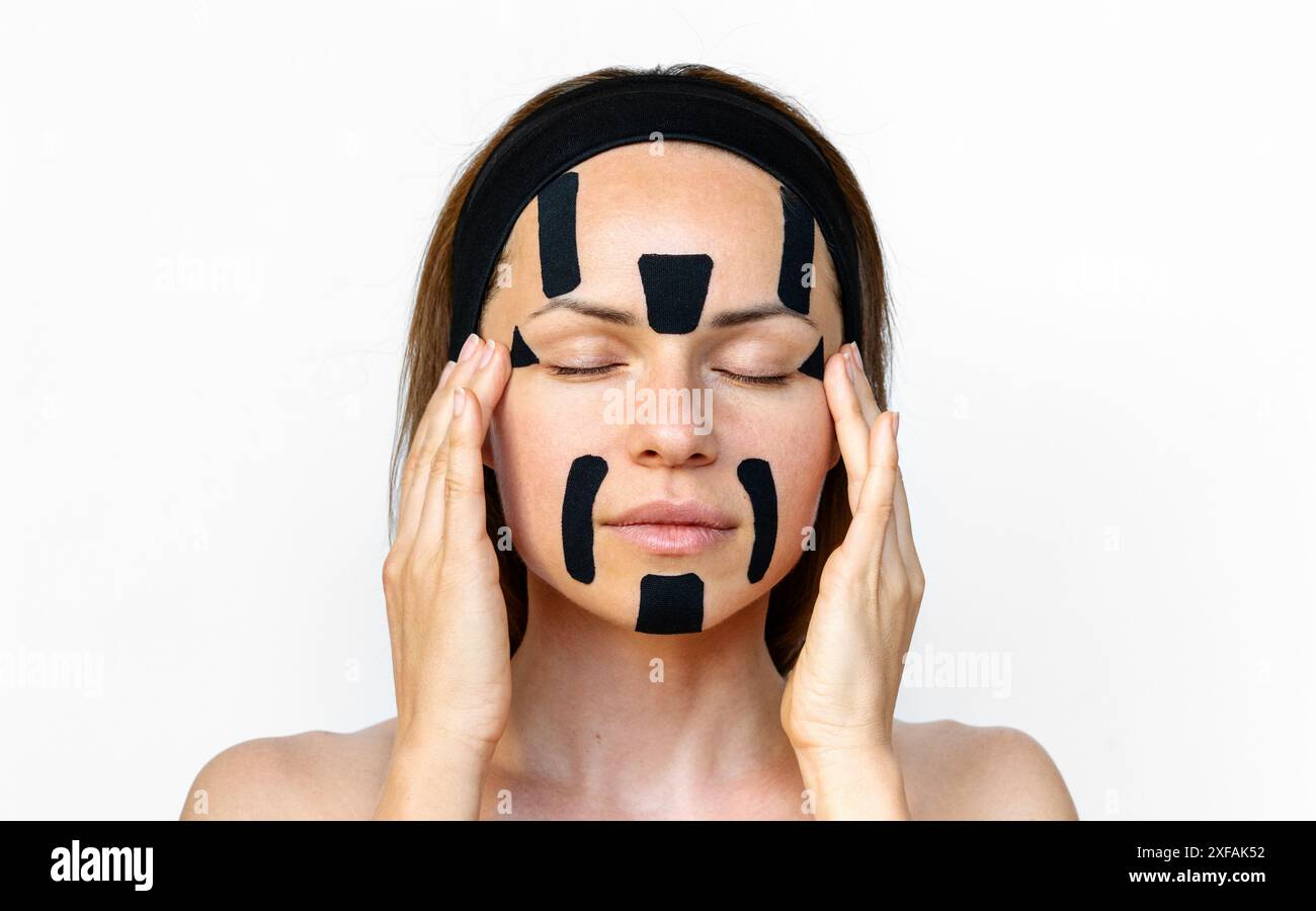 Portrait of a beauty model applying black kinesio tape to her face ...
