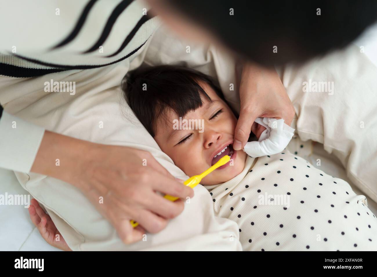mother brushing her little daughters teeth. crying baby with tooth ...