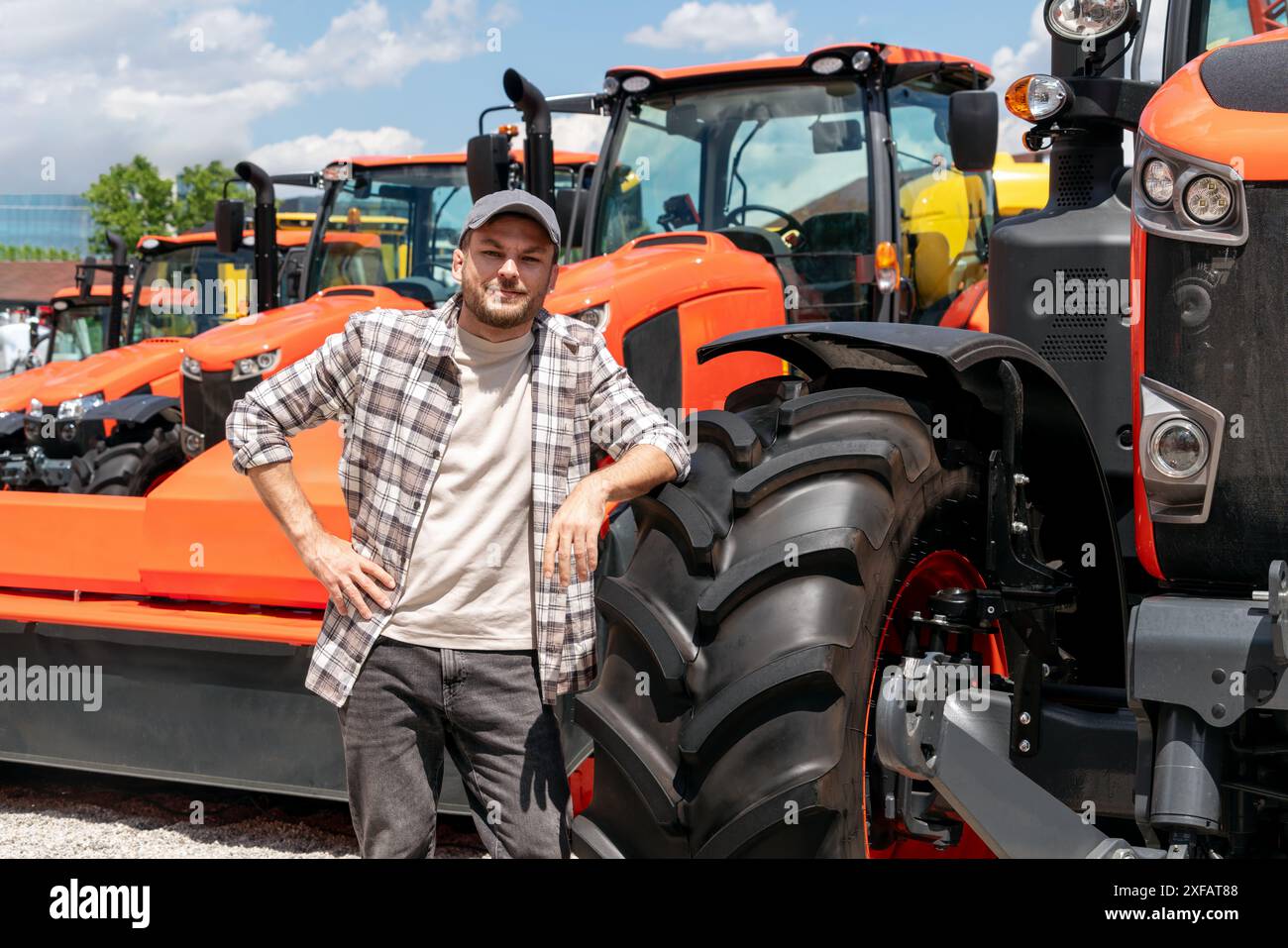 Portrait of a male farmer standing next to a new farm tractor at a ...