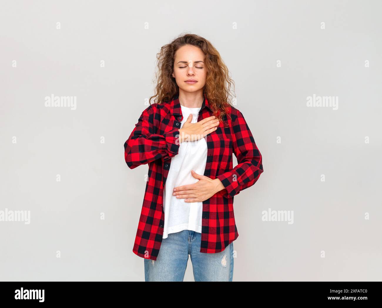 Curly brunette woman in red plaid shirt stands in front of plain wall ...