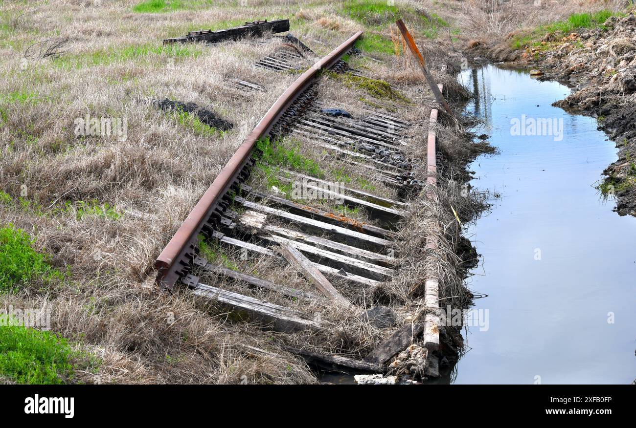 Broken, discarded railroad tracks lay besides ditch filled with water ...