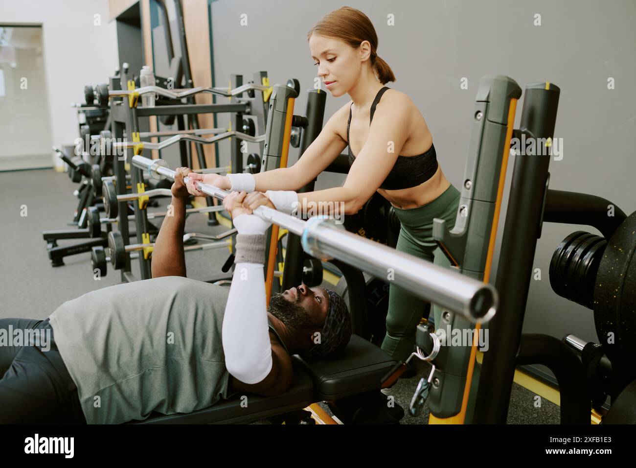 Sporty woman helping her African American friend with bench press using ...