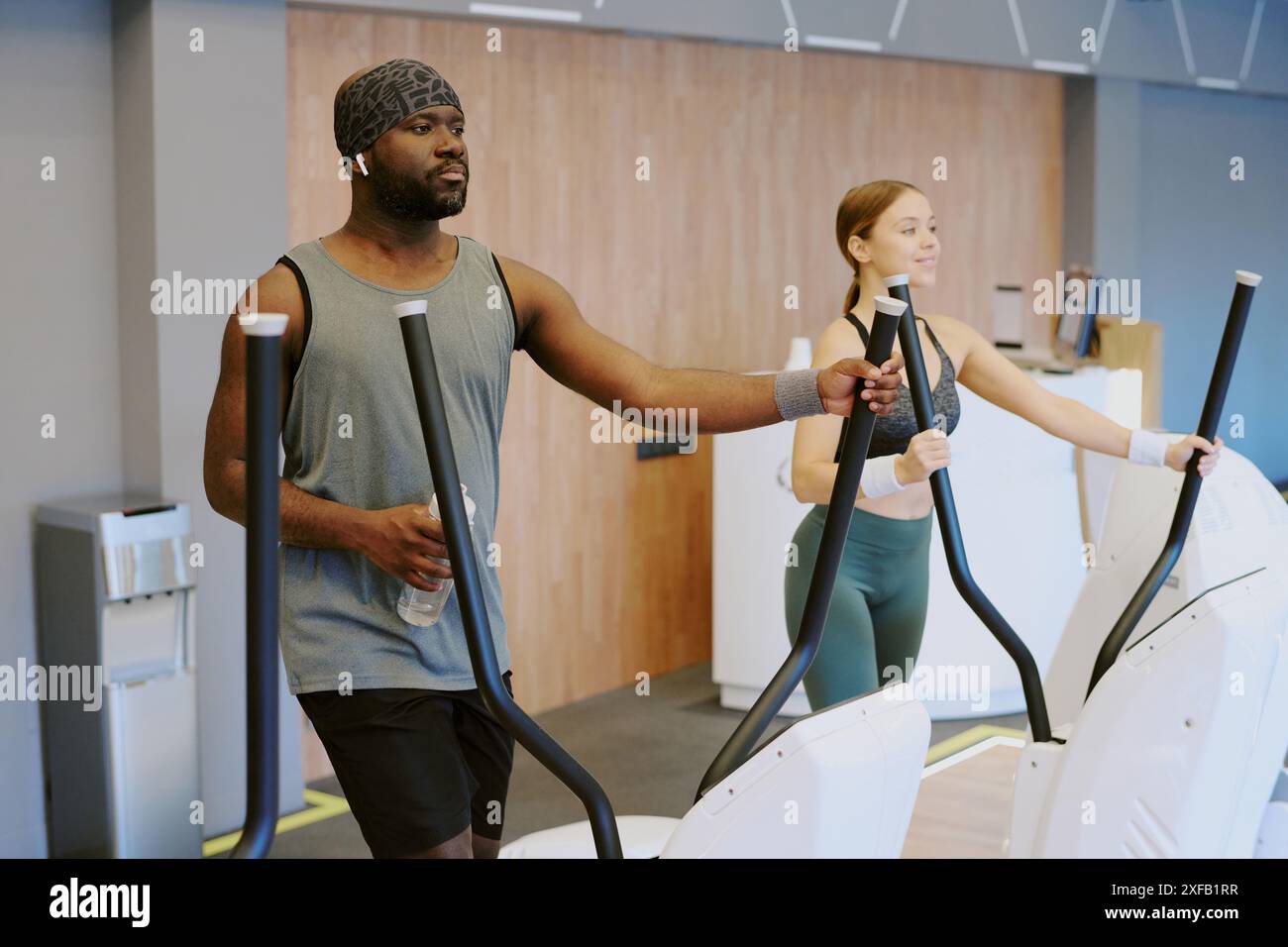 Biracial gym residents running on elliptical machine, pretty woman ...