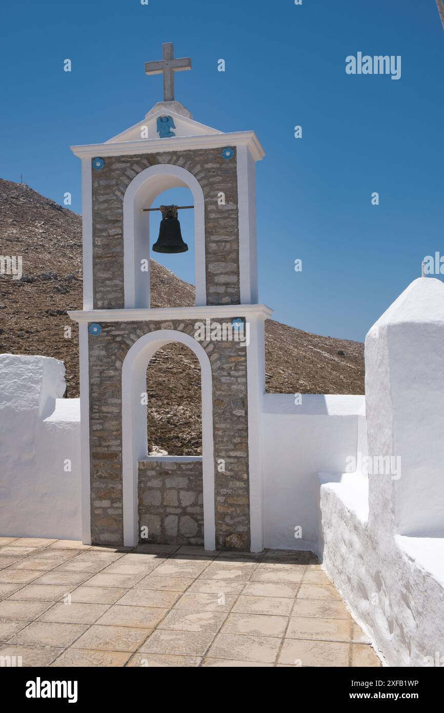 A traditional Greek church bell tower with a cross under a blue sky ...