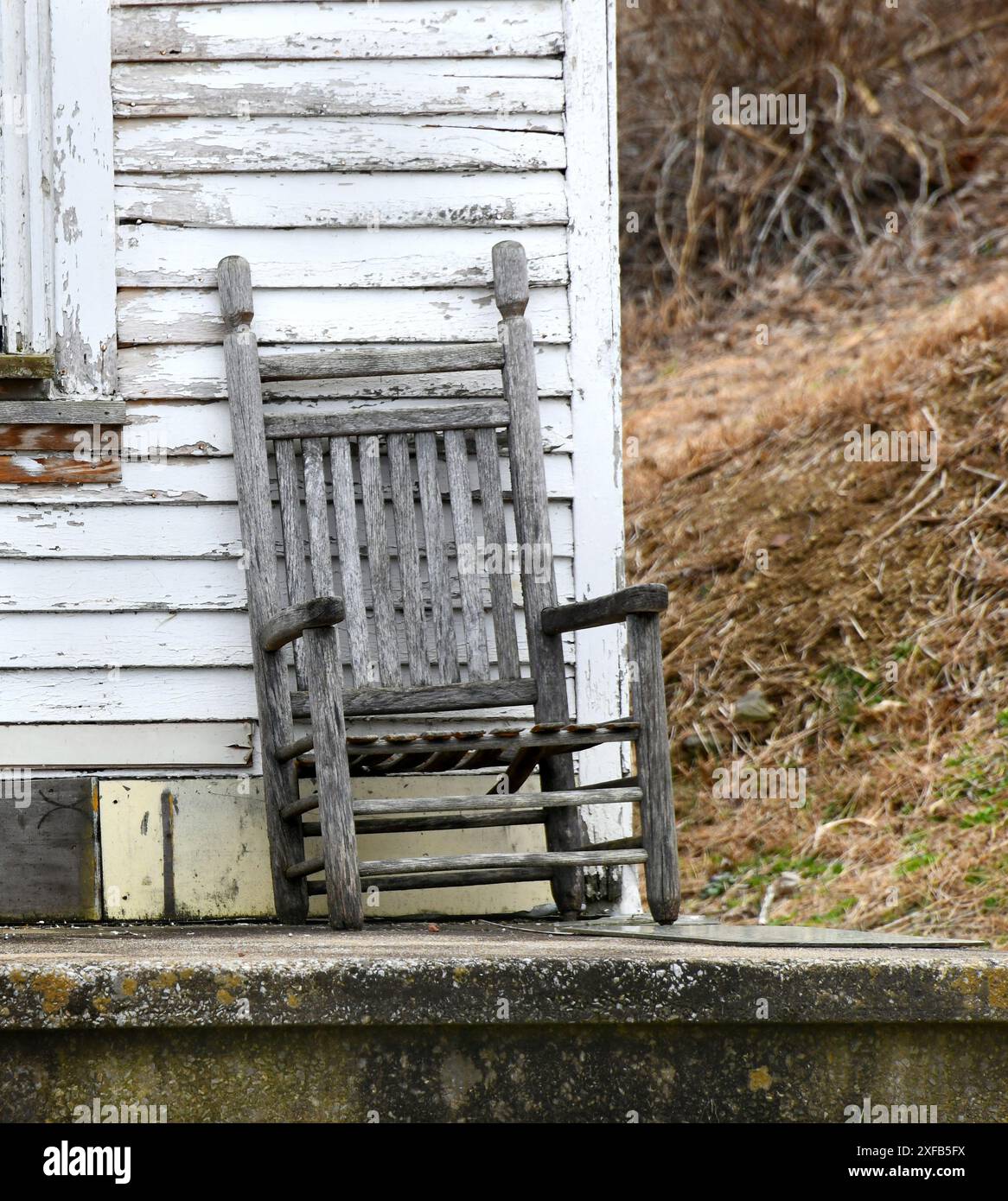 Old wooden and weathered chair sits on the concrete front porch of old ...