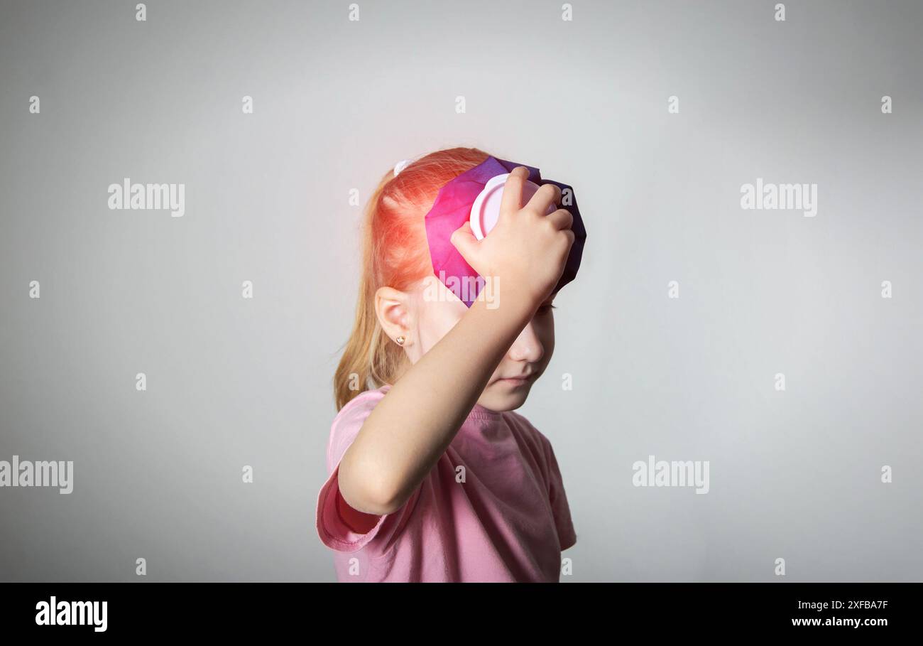 A little girl holds a bag of ice cold against her head. The concept of ...