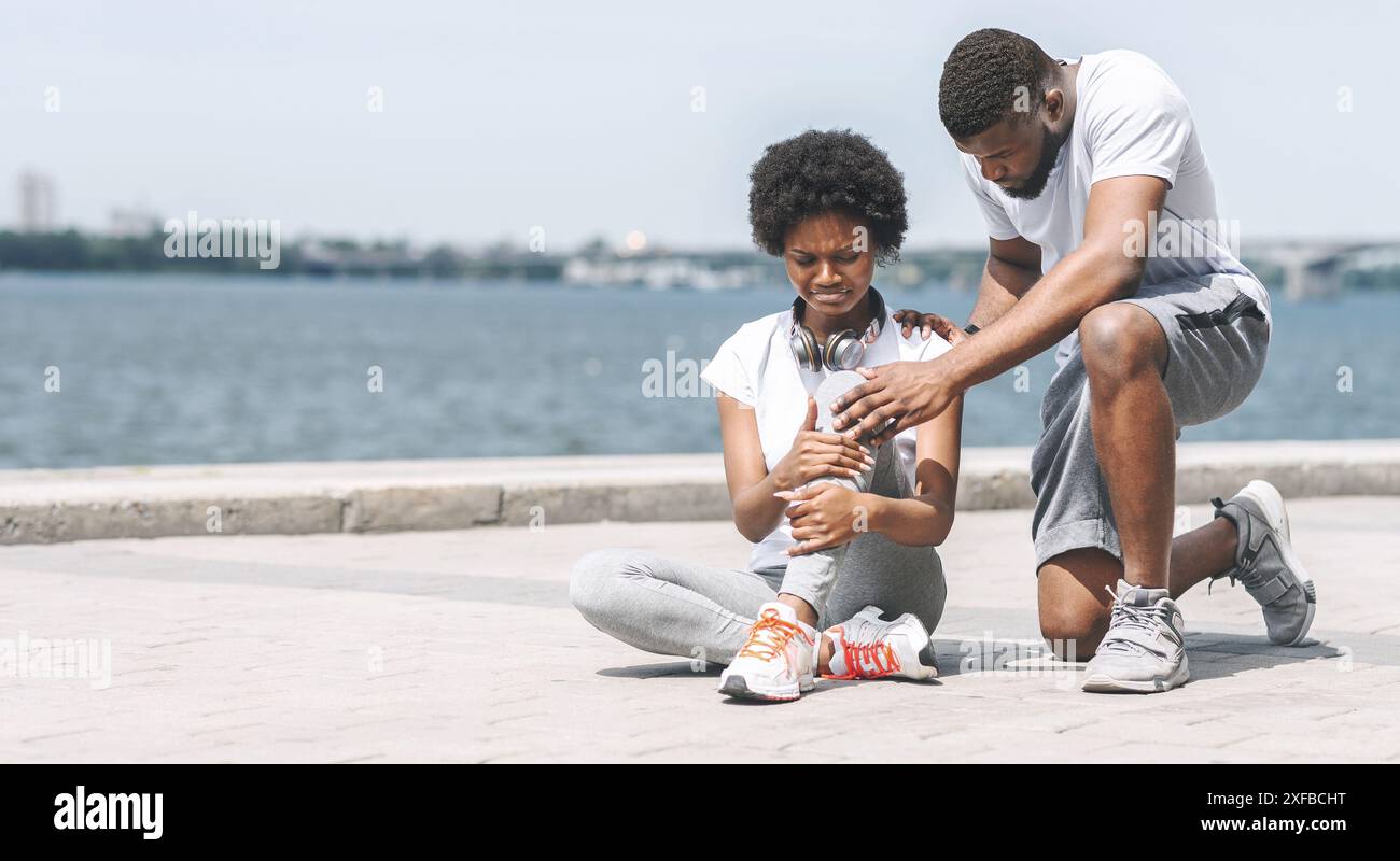 Black Guy Helping Girl Examining Sprained Ankle At Riverbank Stock ...