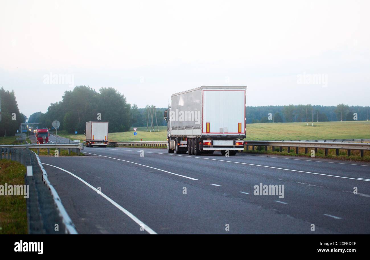 A convoy of semi-trailer trucks transports cargo in the morning during ...