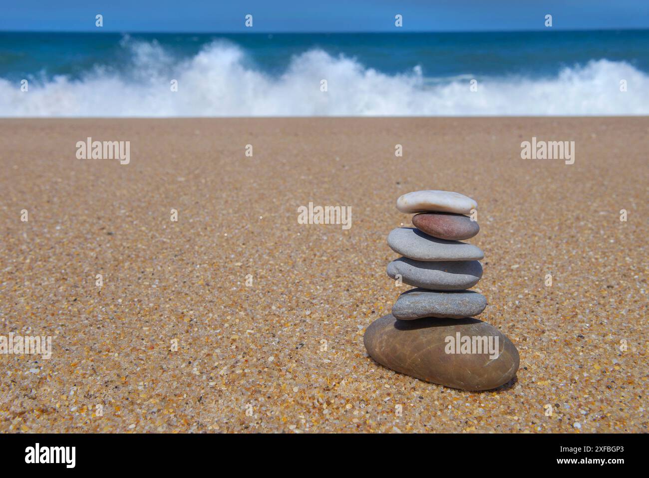 pebbles stacked on a sandy beach in front of ocean and waves background ...