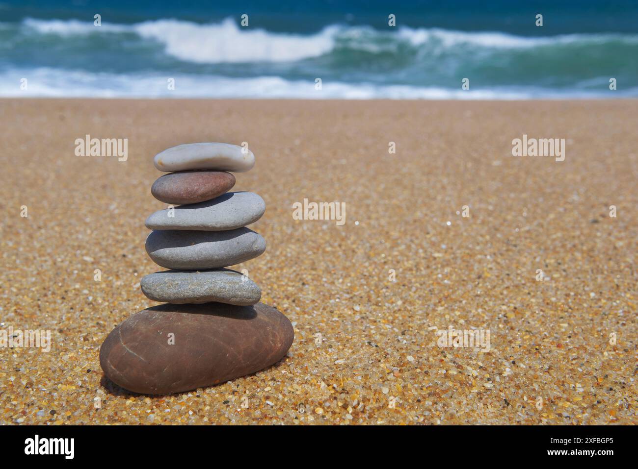 pebbles stacked on a sandy beach in front of ocean and waves background ...