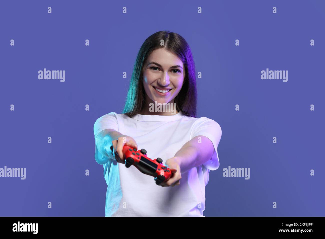 Happy woman playing video games with controller on violet background ...