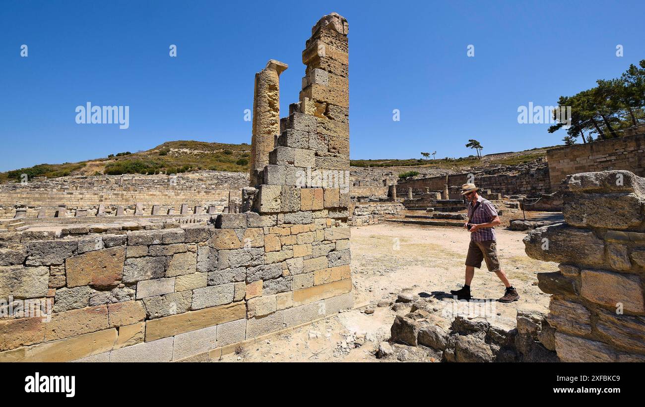 Man walking through a site with ancient stone ruins under a clear sky ...