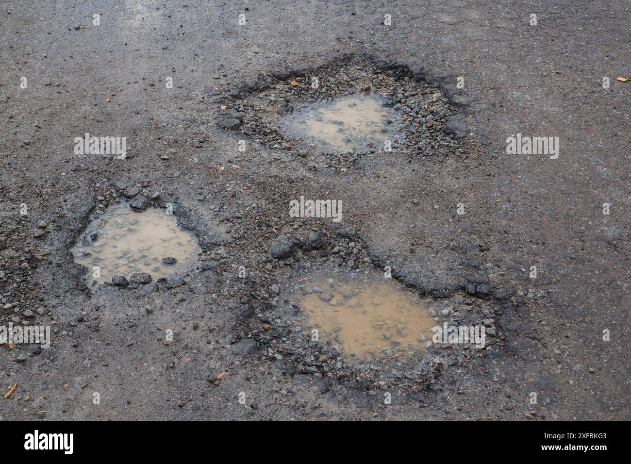 Potholes with rainwater on wet black asphalt road surface in spring ...