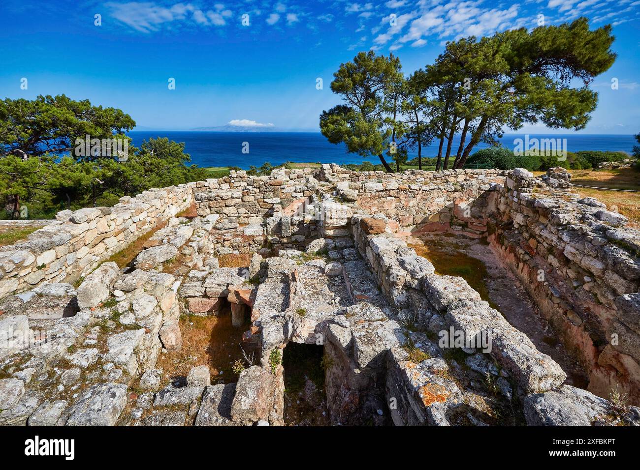Ancient ruins with stone walls and views of the sea and trees under a ...