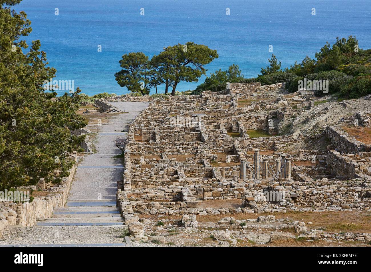 Ancient ruins along a stony path with trees and sea in the background ...