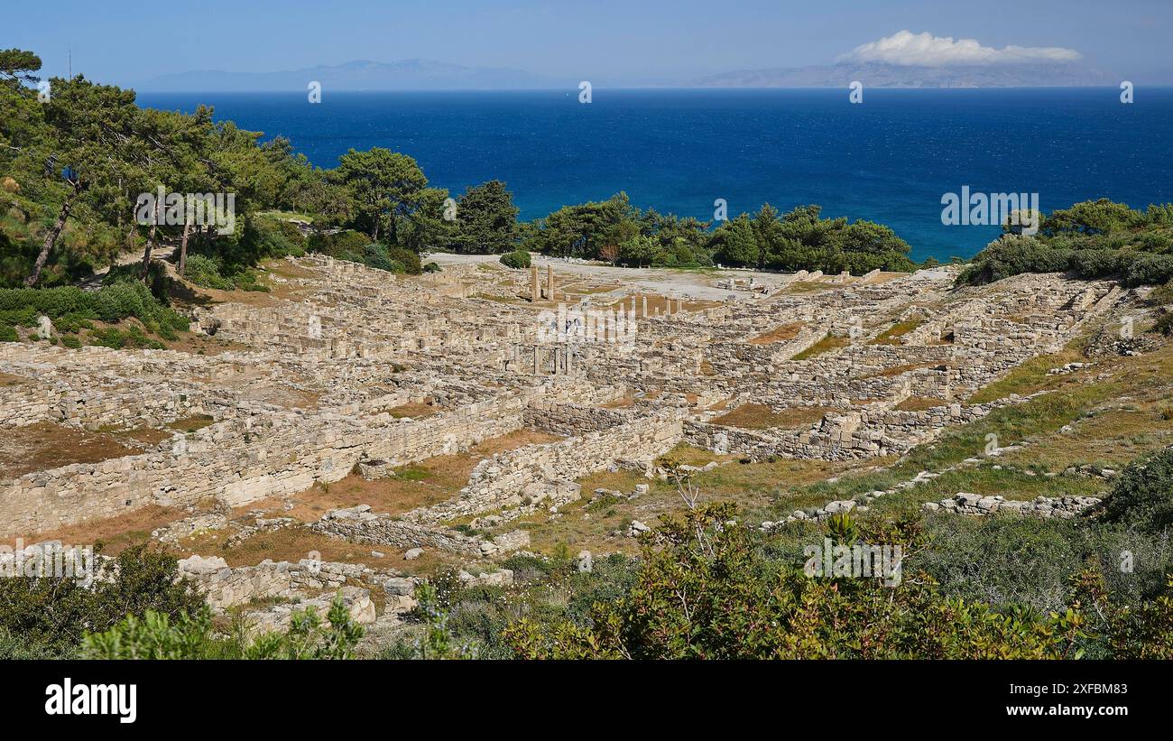 Ruins of an ancient site in front of a blue sea and tree-lined terrain ...