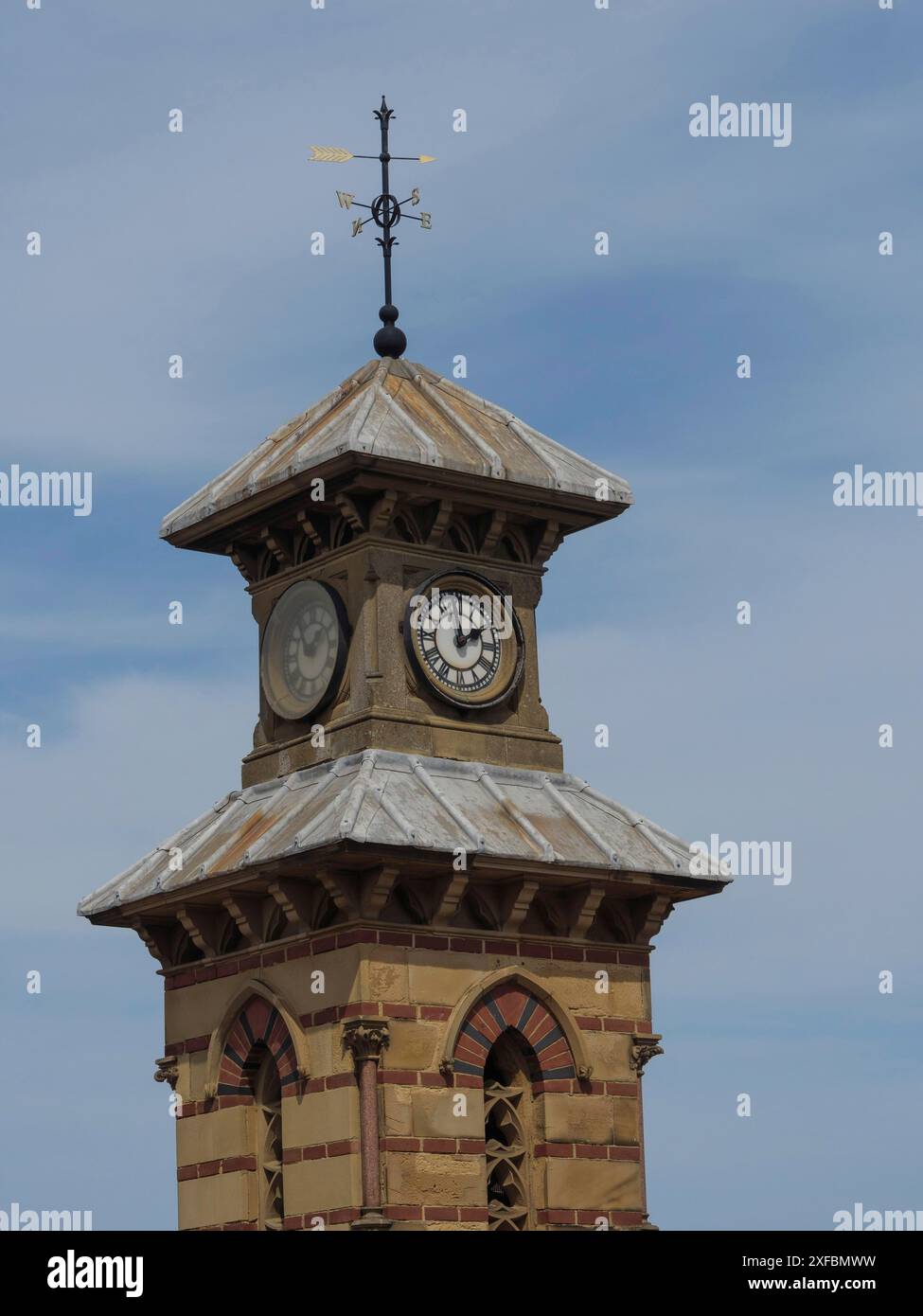 A clock tower with a weather vane against a blue sky shows a historical ...