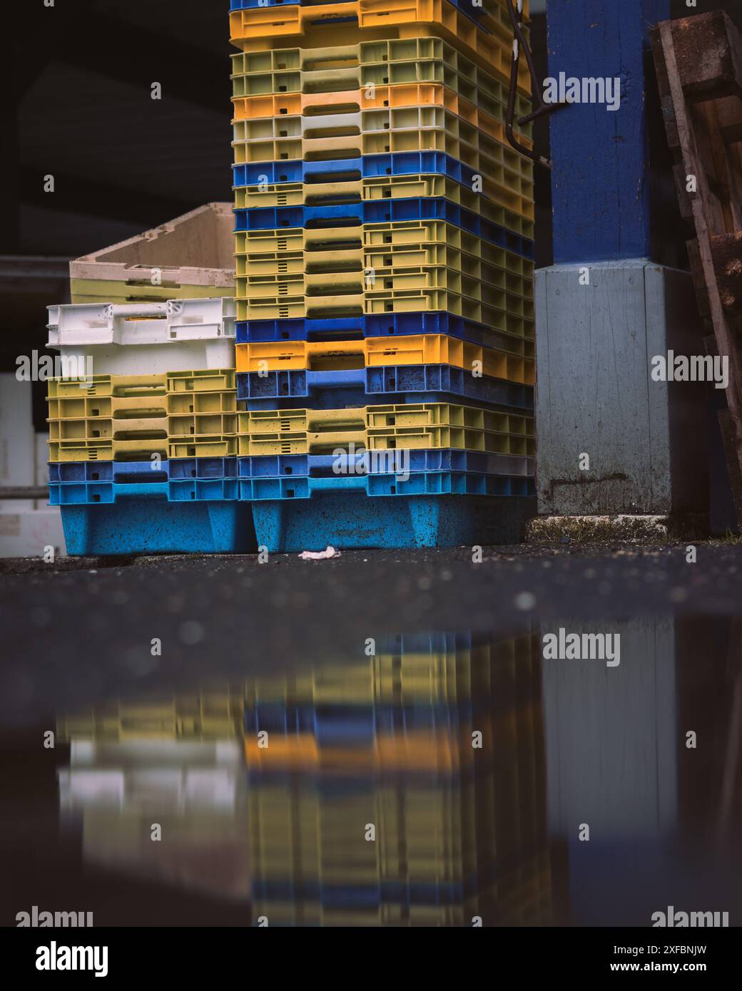 Stack of colorful plastic fisher crates reflected in a puddle in an ...