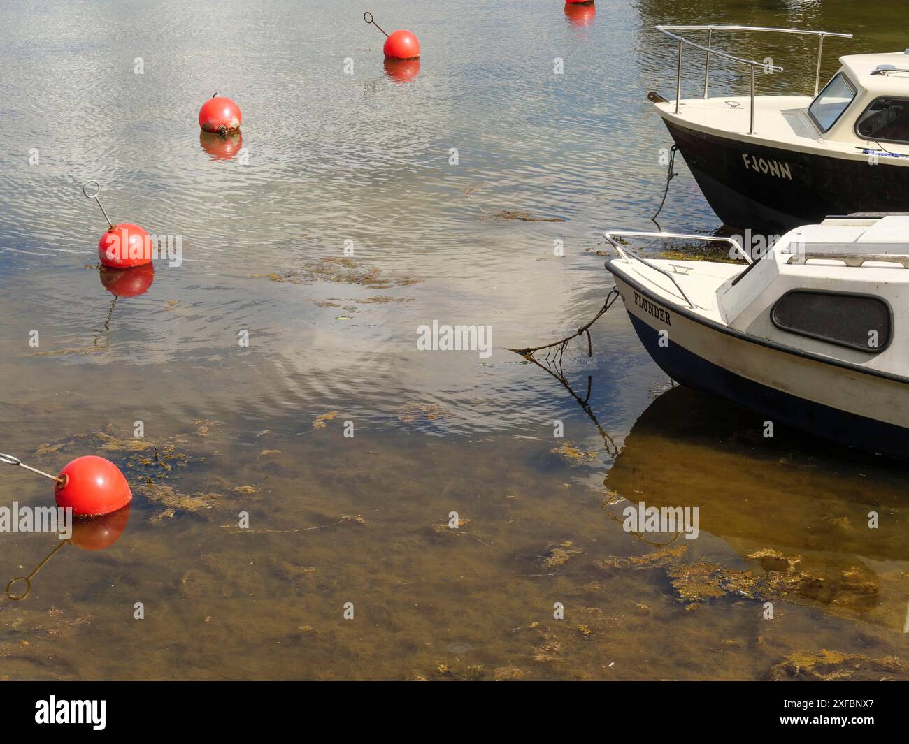 Boats floating in a calm lake with red buoys and clear water reflection ...
