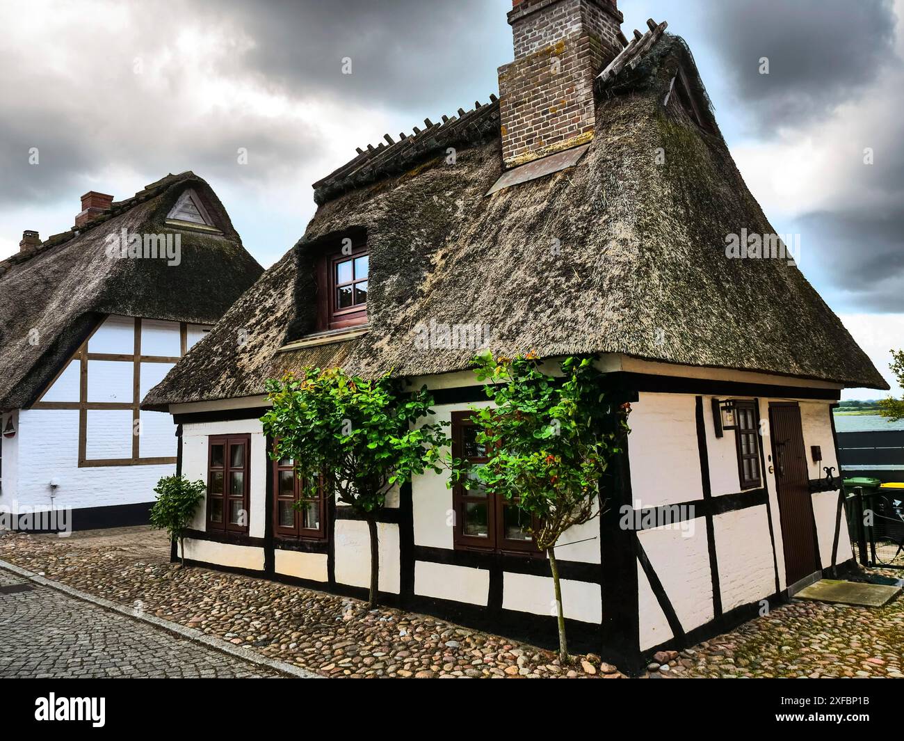 A traditional half-timbered house with thatched roof under a dramatic ...