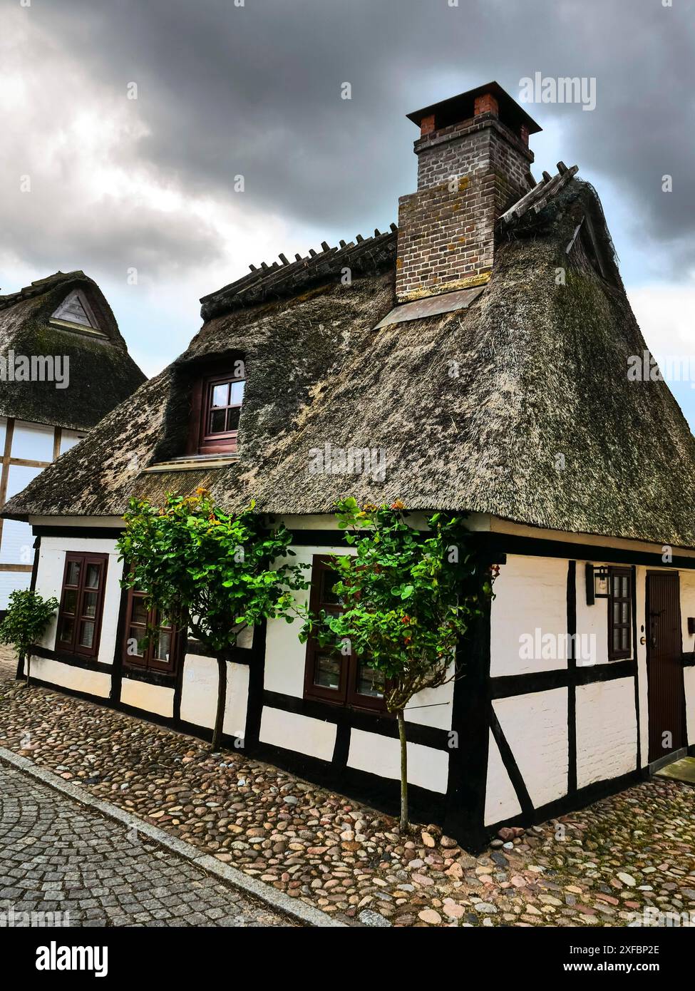Traditional half-timbered house with thatched roof on a cobbled street ...