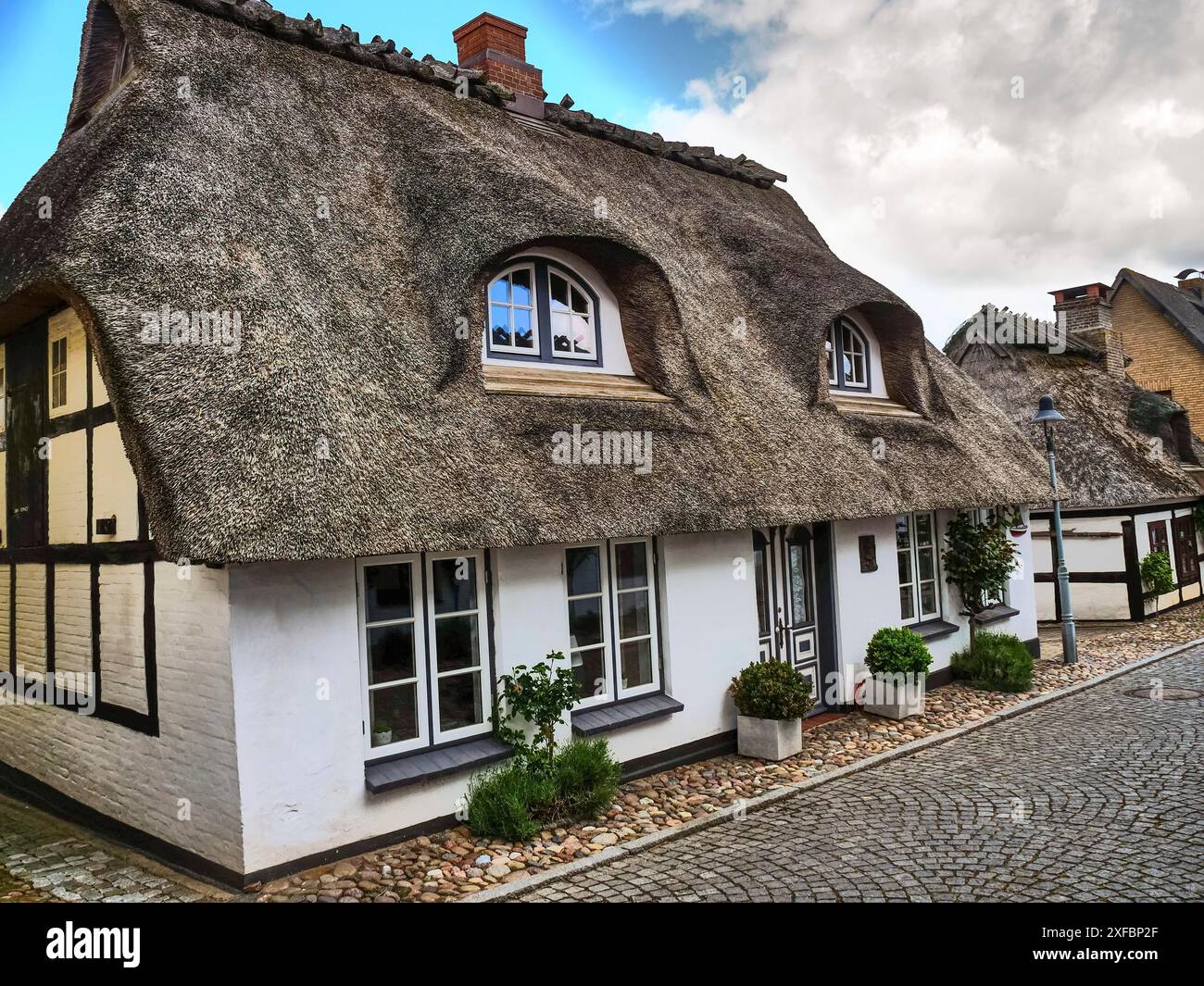 Half-timbered house with thatched roof in a quiet cobbled street in a ...