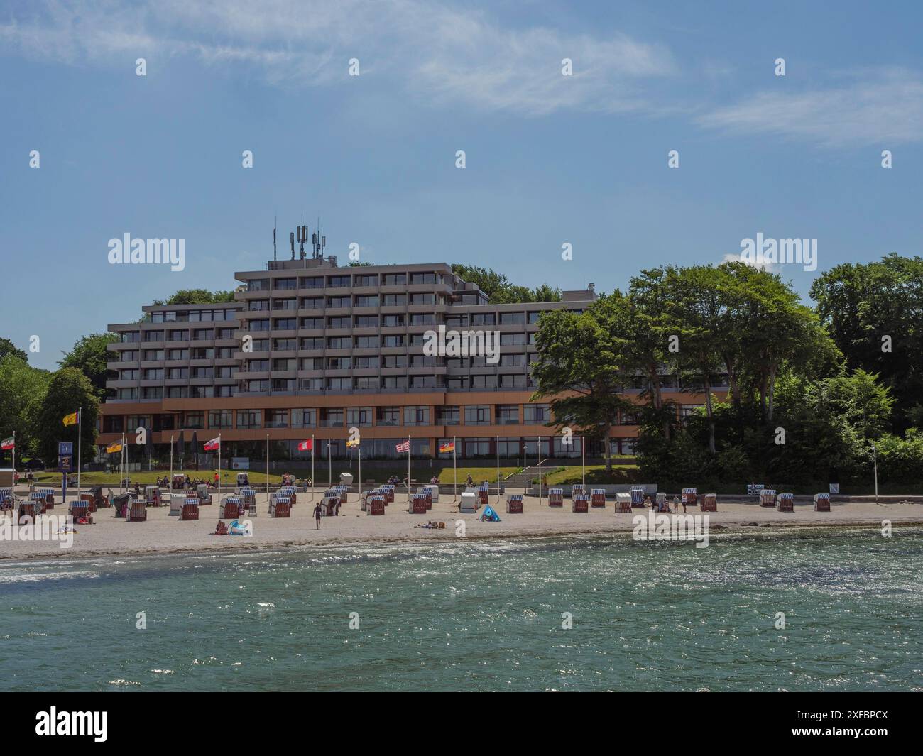 Large hotel on the beach with parasols and bathers under a blue sky, flensburg, schleswig ...
