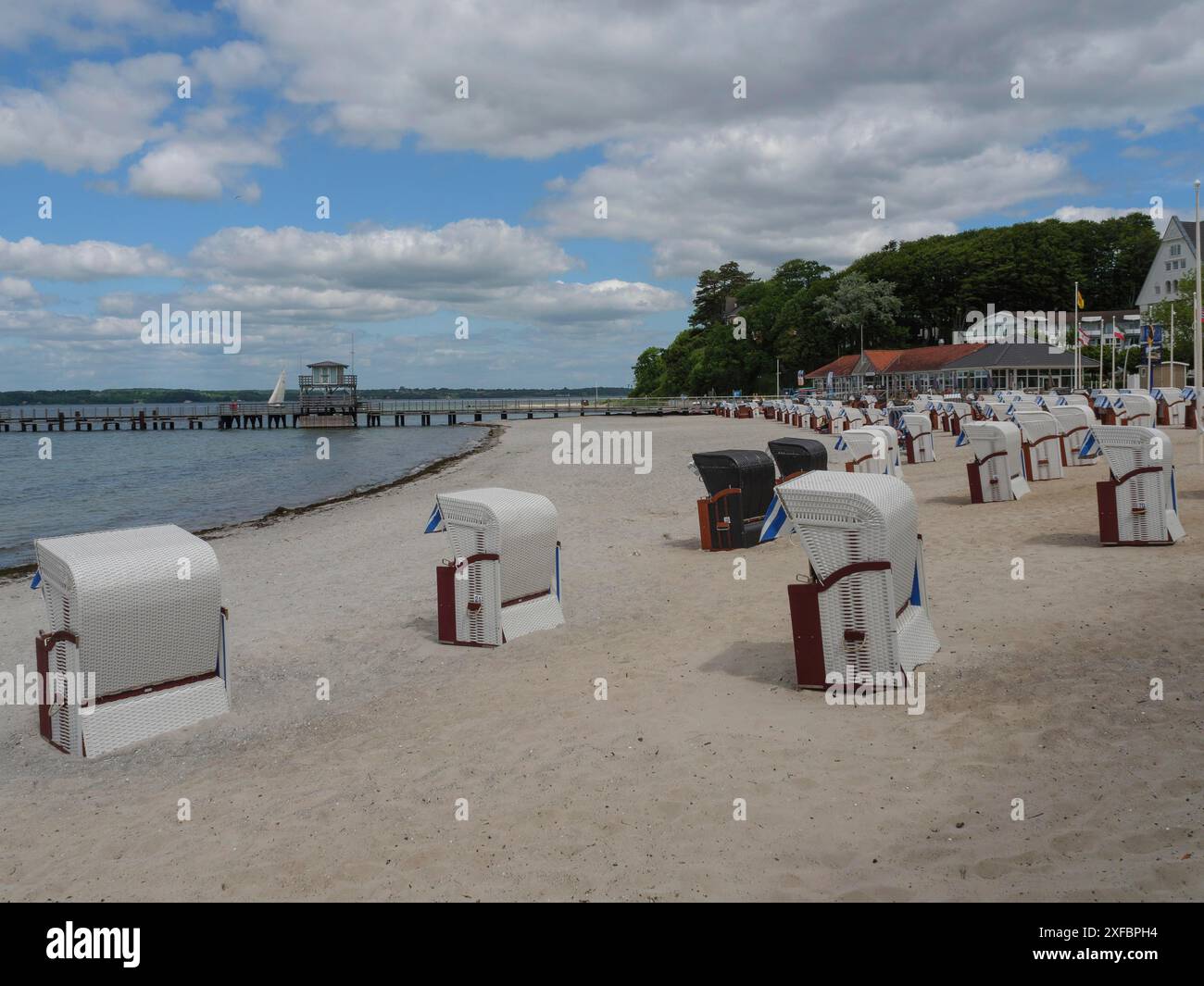 Full beach chairs on the sandy beach near coastal buildings and a pier ...
