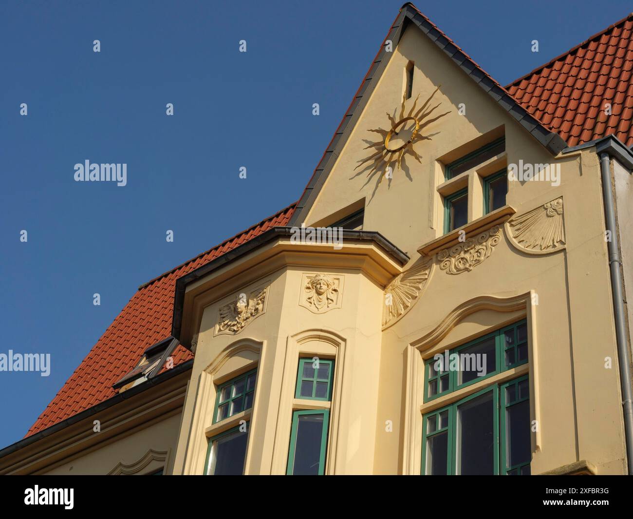 Yellow historic building with sun emblem on the gable and green windows ...