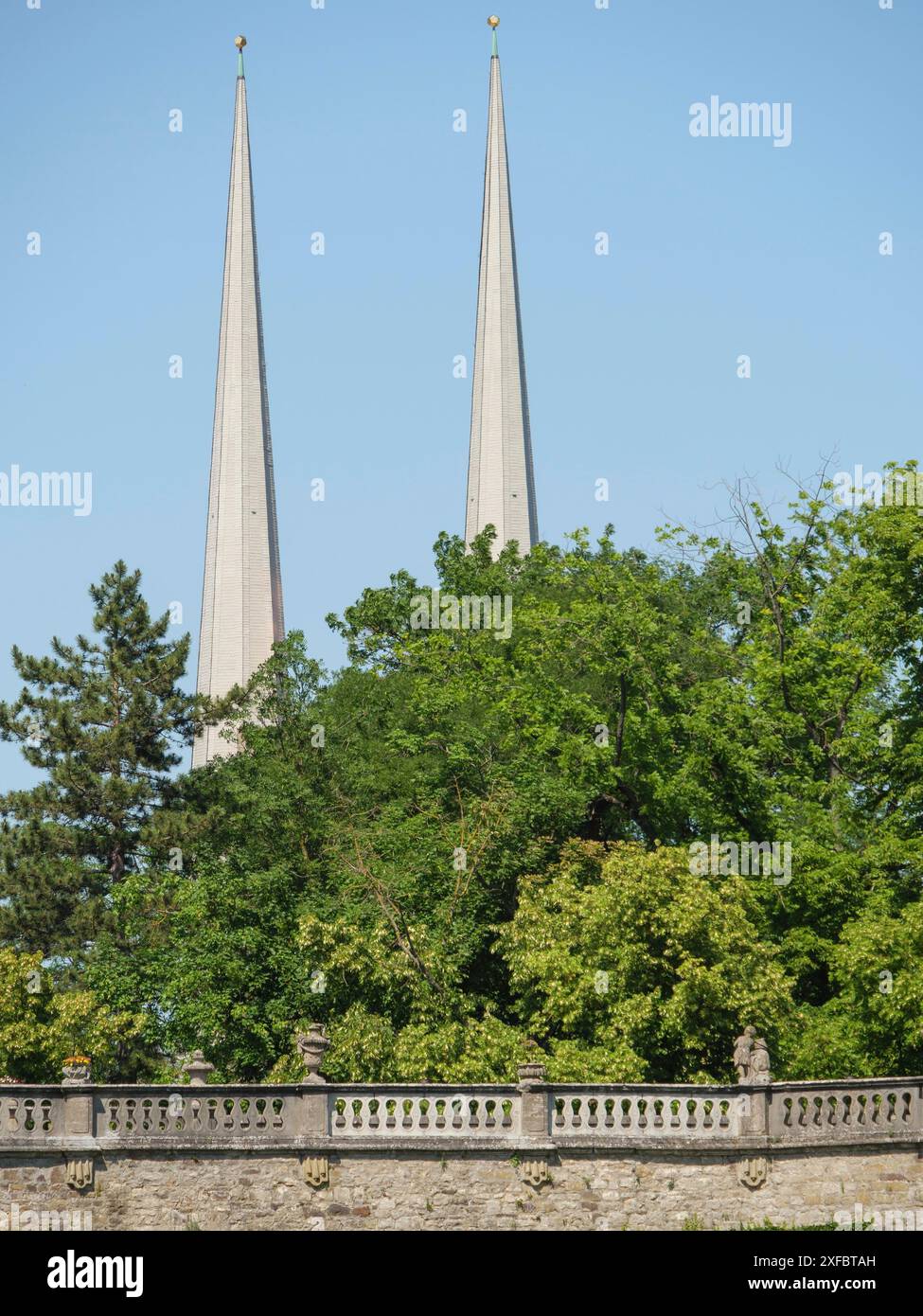 Two tall church towers rise majestically above green trees and a ...