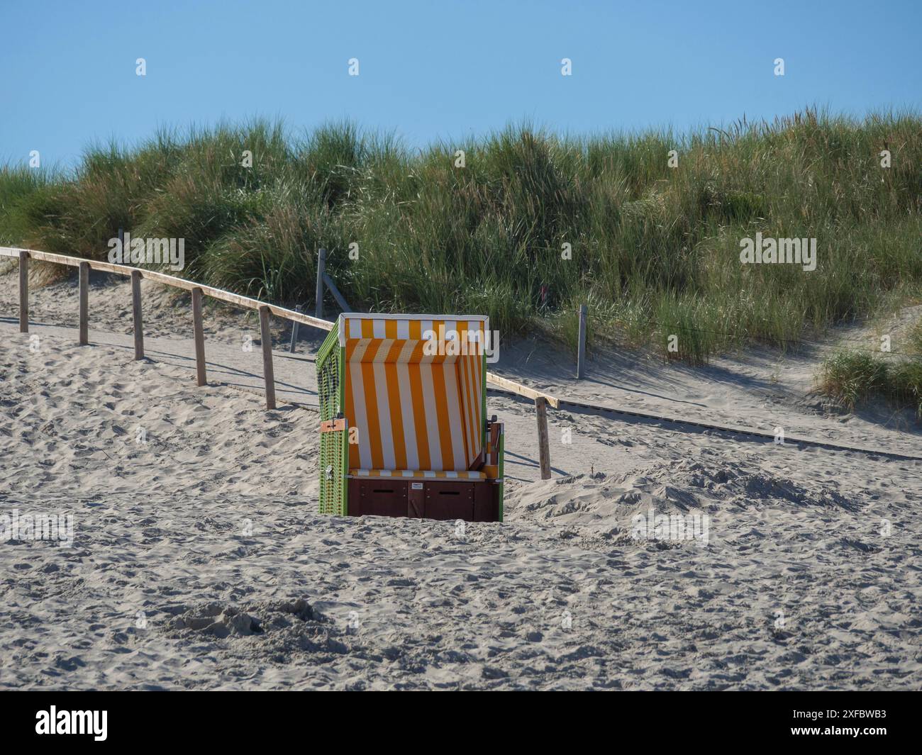 A single beach chair stands on the sandy beach in front of grassy dunes ...