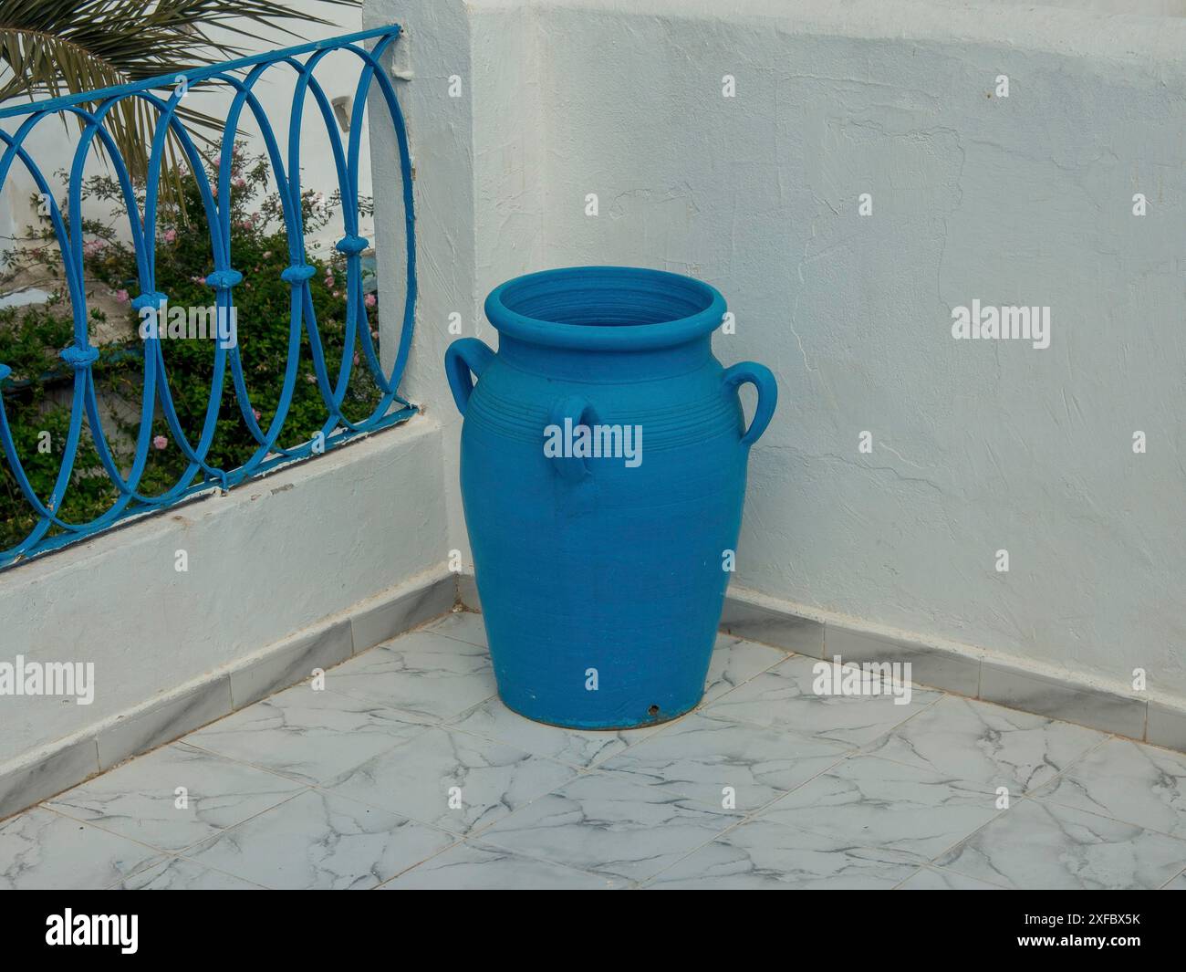 A blue ceramic jug stands on a terrace surrounded by white walls and a ...