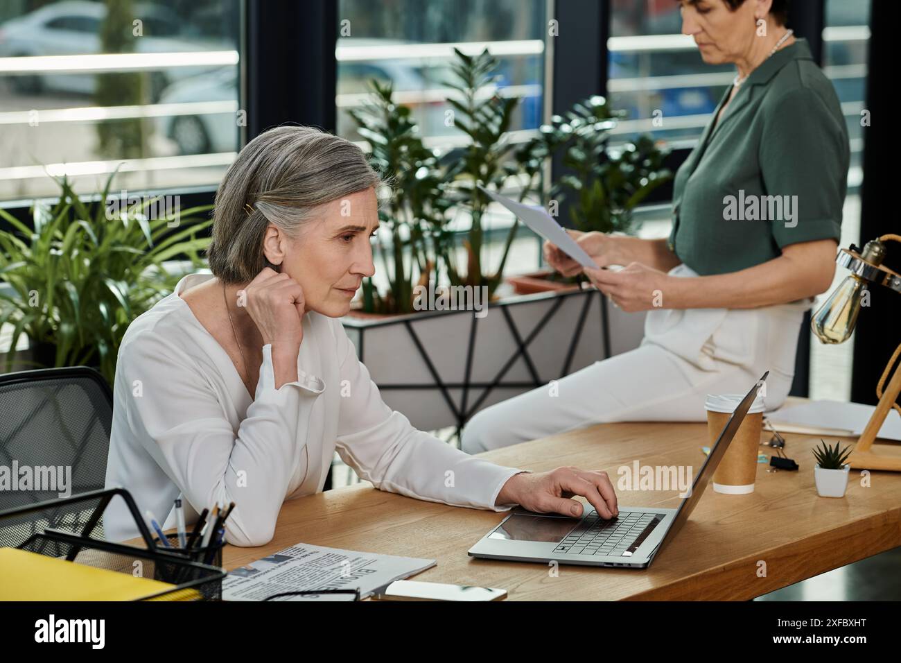 Two women, sitting at desk with laptop and working with papers Stock ...