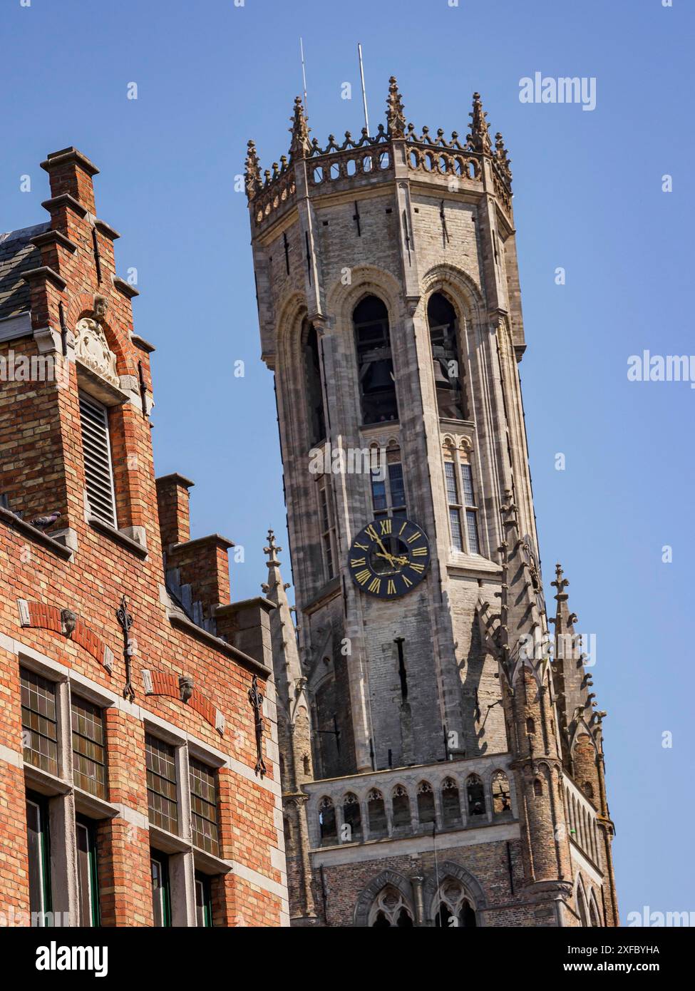 A Gothic bell tower with clock next to historic brick buildings, Bruges ...