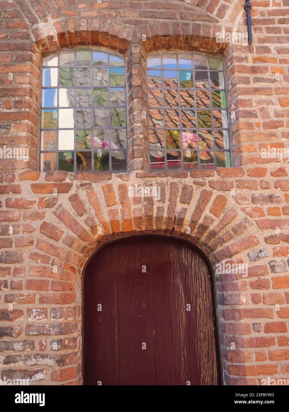 Brick wall with arched door and scenes reflected in windows behind it ...