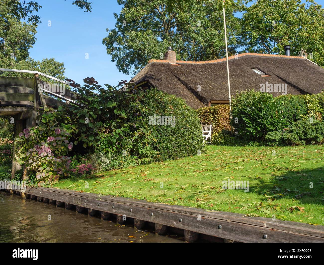 House with thatched roof and lush garden, wooden bridge over the canal ...